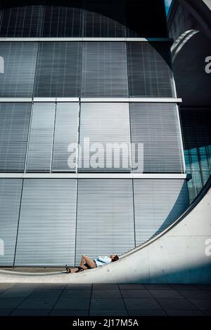 Businessman lying on wall in front of modern building Stock Photo - Alamy