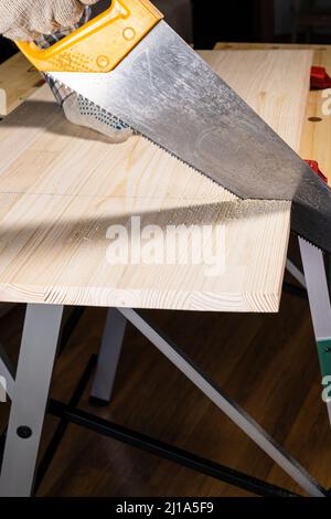 side view of carpenter saws wooden board with hand saw on workbench at ...