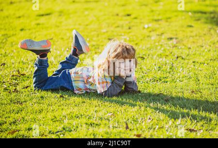 Child liyng outdoor. Kid in park. Spring Boy lie down on grass. Summer ...