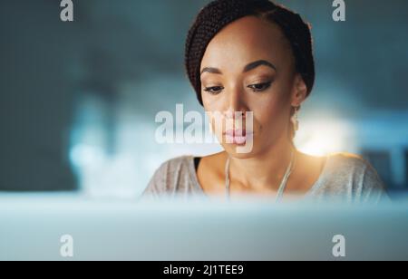 Putting in the hours. Cropped shot of a young businesswoman using her ...