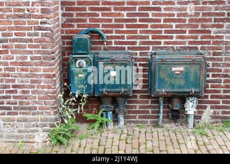 old weathered green power boxes in front of a red brick wall overgrown ...