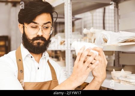 A young attractive male potter with a beard and mustache works in his ...