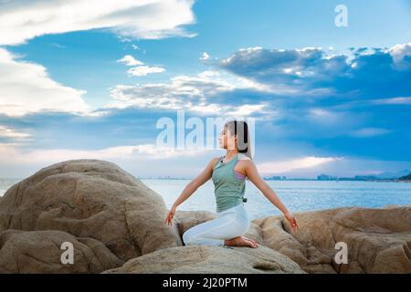 Beautiful young lady practicing yoga on the beach reef - stock photo ...