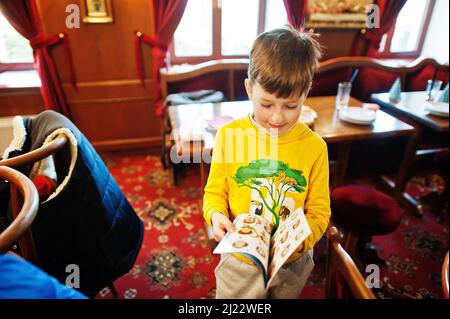 Child blond boy reading magazine in the park, sitting onthe green grass ...