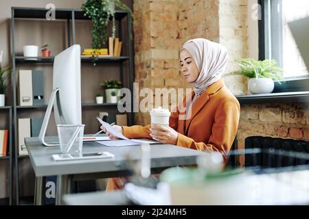Young serious female broker or analyst making notes during data ...