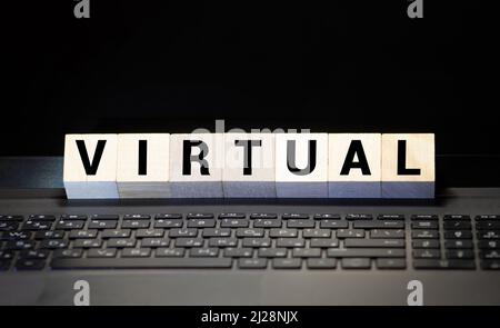 The word VIRTUAL is written on a wooden block on a computer keyboard ...