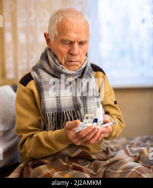 Gray-haired man in his 80s puts on a hat while standing in the living ...