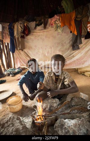 Three children warm themselves by the fire in their one room shack in ...