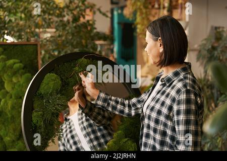 Designer gluing green plant on round mirror Stock Photo - Alamy