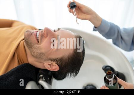 Beautician applying hair serum on mans head Stock Photo - Alamy