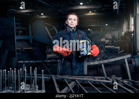 Worker girl with welding on steel structure in factory, light spark ...