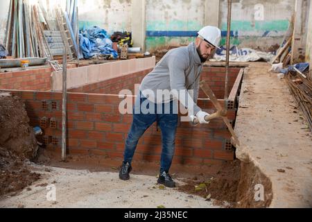 Guy excavating ground with mattock at building site Stock Photo - Alamy