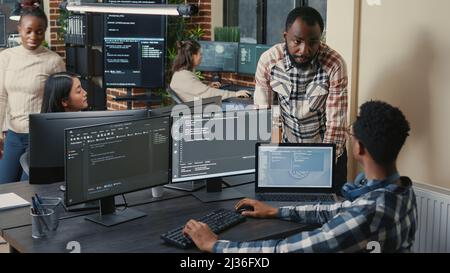 Programer working at desk with multiple computer screens and laptop with green screen chroma key ...