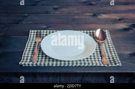 White plate on a checkered doily on a dark wooden table. Vintage ...
