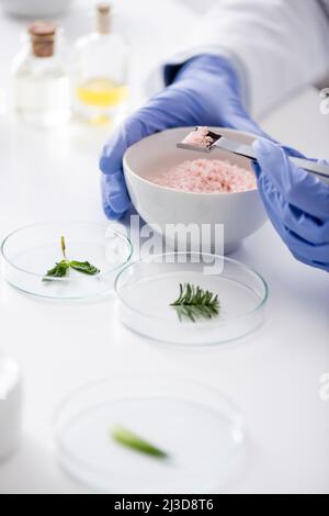 cropped view of chemist in latex glove holding bowl with cream near ...