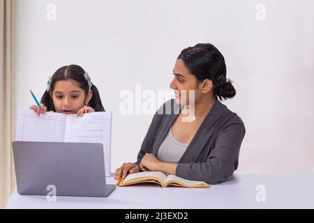 Girl submitting homework through online class using laptop and mother sitting beside Stock Photo ...