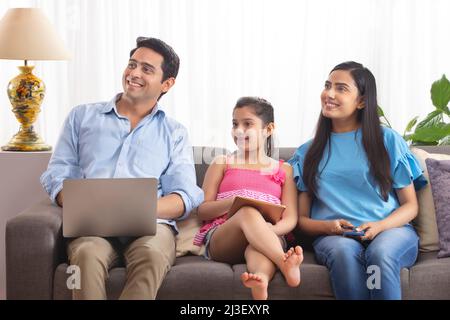 Family members looking elsewhere while sitting on sofa in living room ...