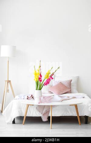 Vase with gladiolus flowers, lamp and decor on commode near white brick ...