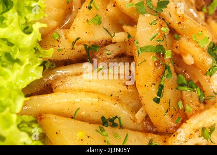 Delicious crispy fried potatoes in slices on a black ceramic plate ...