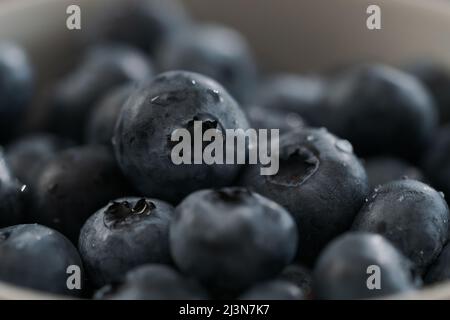 Closeup shot of washed blueberries in white bowl on wood table, shallow ...