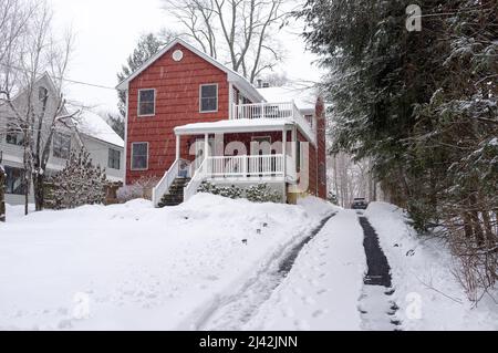red suburban house with front yard and driveway covered with snow after ...