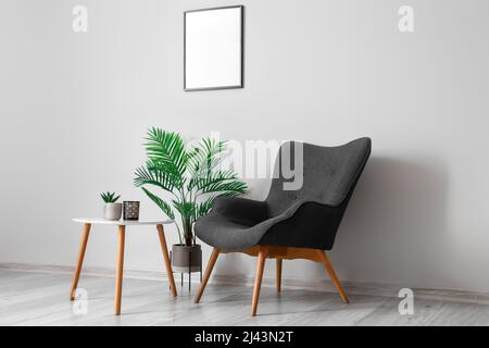 Stylish armchair with table and plants near light wall Stock Photo - Alamy