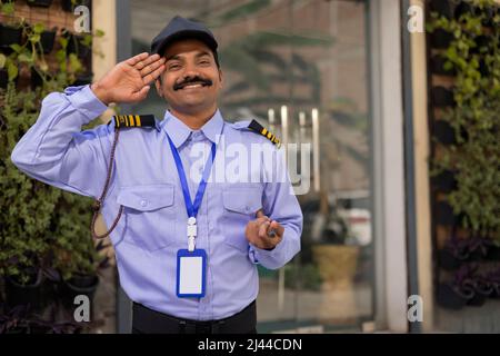 Portrait of security guard saluting while working at gate Stock Photo ...