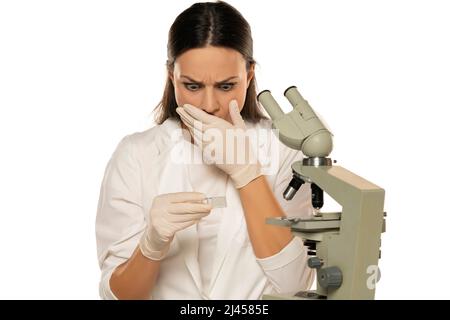 Portrait of shocked female scientist with microscope on a white ...