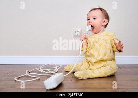 Toddler baby boy gnaws electrical wires while sitting on the floor ...