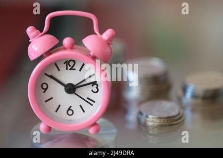 Pink alarm clock compass and stacks of coins closeup Stock Photo - Alamy