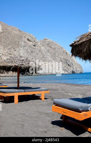 Sun beds and a sun umbrella at the famous black sandy beach of Perissa ...