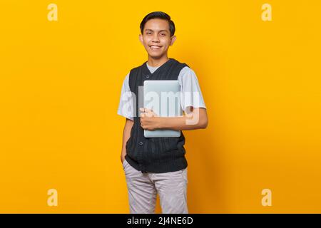 Portrait of Cheerful Asian man bring laptop over yellow background ...