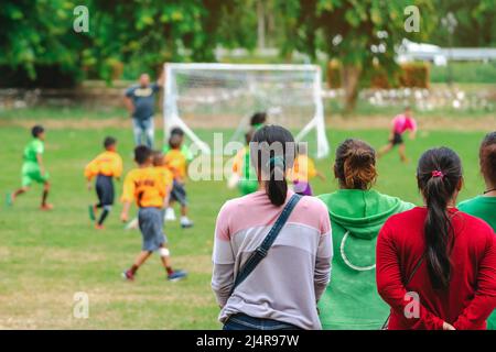 Back view of Mom watch and cheering her son playing football in school ...