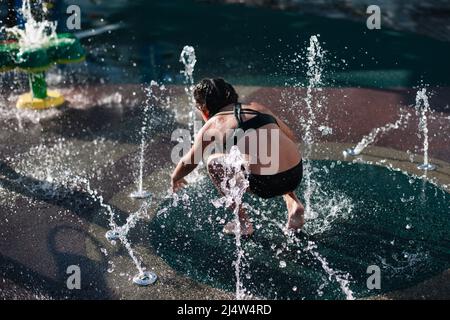 Girl playing in jets of water fountain, seen through sprays and ...