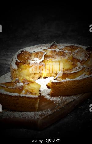 Apple tart covered in icing sugar on a wooden chopping board. With ...