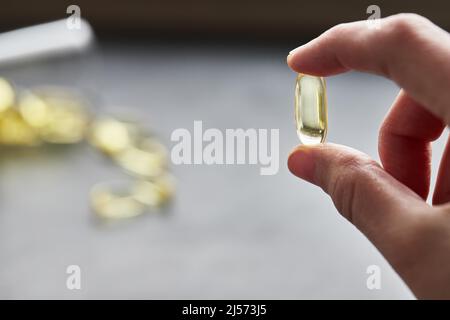 Man holds fish oil capsule close to mouth while looking at jar Stock ...