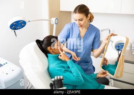 Latin woman holding mirror during cosmetologist's examination Stock ...