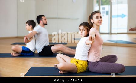 Tween girl with mother doing exercises in pair during family yoga ...