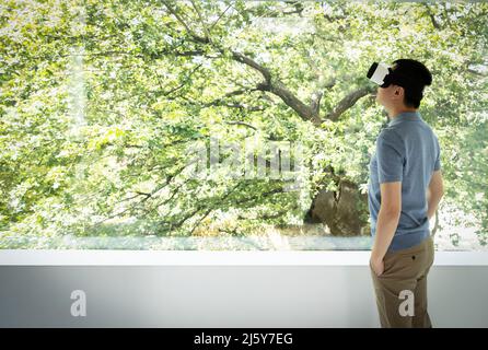 Man using VR headset at window with view of tree Stock Photo - Alamy