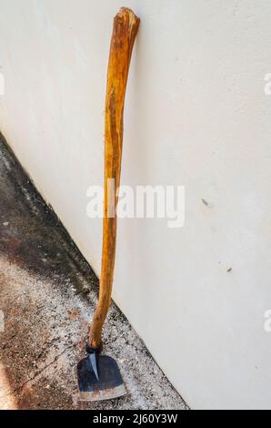 A black hoe with long wooden stick is leaning against a wall outside ...