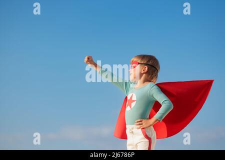 Superhero child playing outdoor. Super hero kid against blue summer sky ...