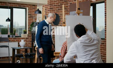 Art class teacher guiding senior student to draw sketch on canvas. Old ...