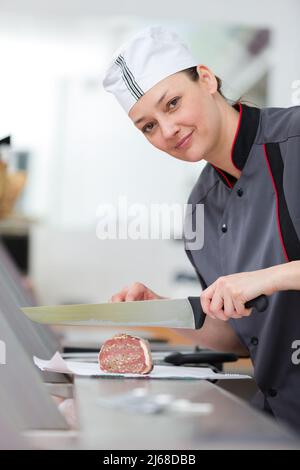 Pretty butchery woman cutting ham with knife Stock Photo - Alamy