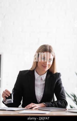 blonde notary holding stamper while working with documents in office ...