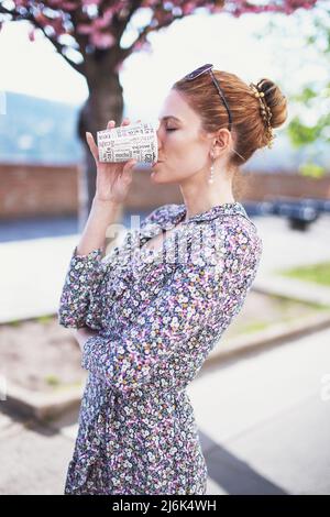 Young redhead woman drinking coffee waiting for washing machine at ...