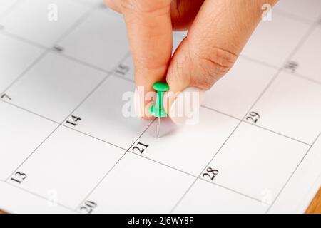a woman's hand holds a green button to mark the date on a white ...