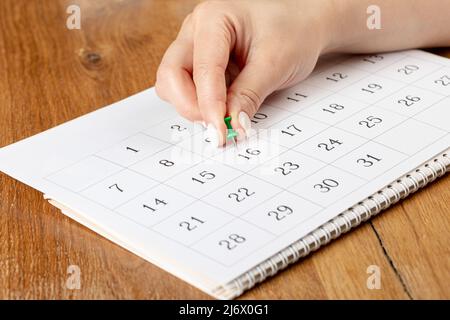a woman's hand holds a green button to mark the date on a white ...
