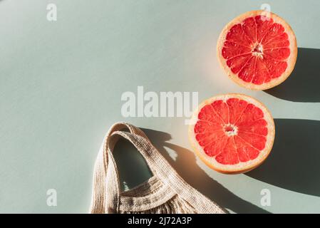 Fresh red grapefruit, mesh bag and herbs in sunlight. Top view, flat ...