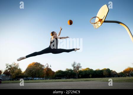 Female ballet dancer shooting baskets on an outdoor Basketball court ...