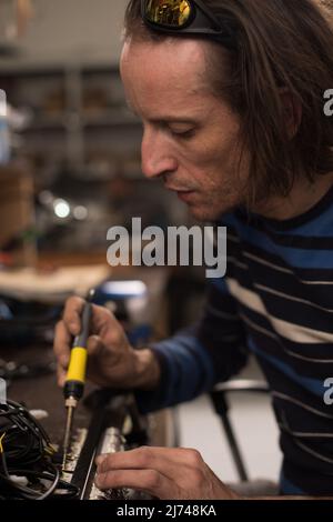 Industrial worker man soldering cables of manufacturing equipment in a ...